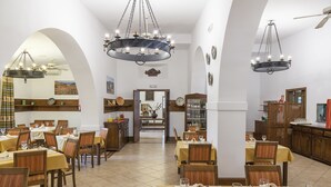 Uma sala de jantar com várias mesas preparadas para hóspedes, com lustres e cadeiras de madeira.