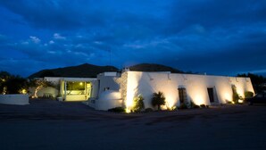 Um edifício moderno com entrada de vidro e fachada branca, cercado por um estacionamento e palmeiras.