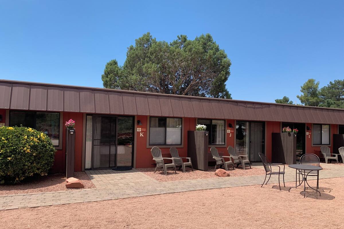 Um motel com fachada vermelha, várias janelas e área externa com mesas e cadeiras.