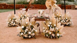Decoração de casamento ao ar livre com um arco de madeira rústico, arranjos florais e luzes de corda, com o cenário do deserto ao fundo.