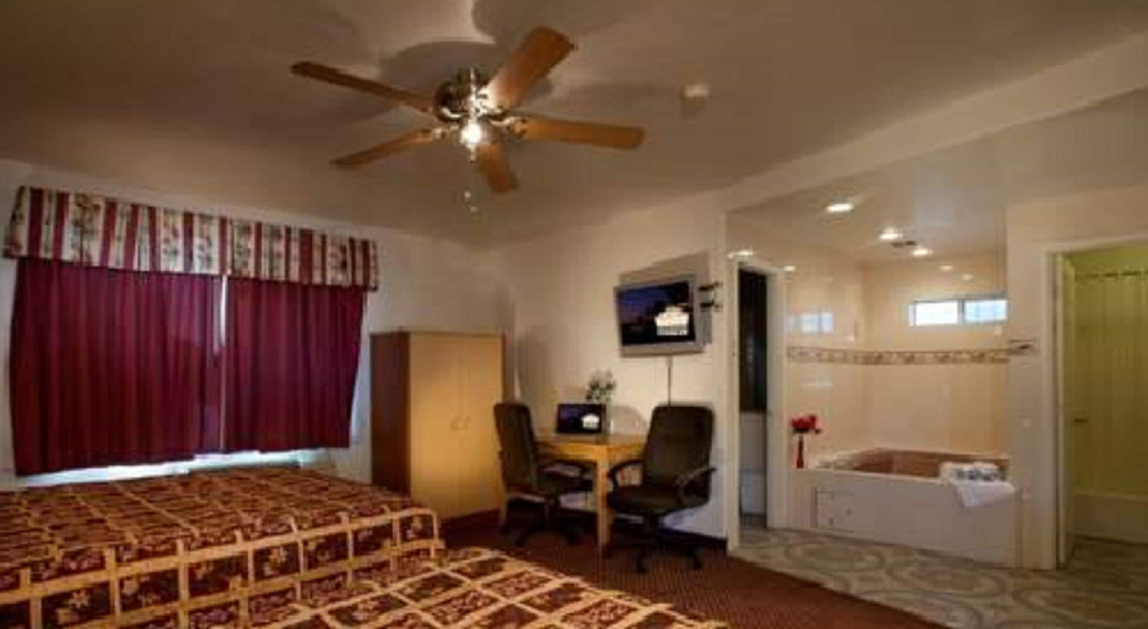 Quarto de hotel com cama, escrivaninha, cadeira, ventoinha no teto, televisão e banheiro com banheira.