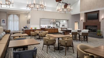 Um saguão de hotel moderno com área de refeições, cozinha e lareira.