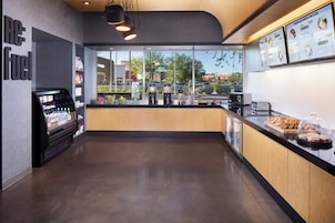 Interior moderno de café com máquina de bebidas de serviço próprio, balcão com doces e um quadro de cardápio.
