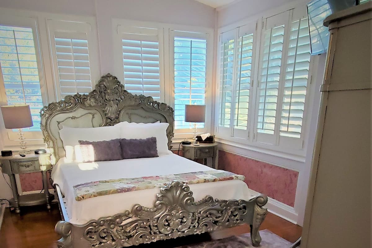 Um quarto com uma cama grande e ricamente decorada, piso de madeira e tapete rosa.