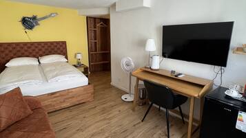 Quarto de hotel com cama, secretária, televisão, ventoinha e guarda-roupa.