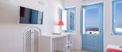 Quarto com uma escrivaninha branca, luminária vermelha, TV e porta que dá para uma varanda com vista.