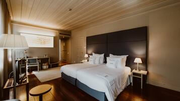 Quarto de hotel moderno com uma cama grande, mesas de cabeceira, escrivaninha e uma cadeira.