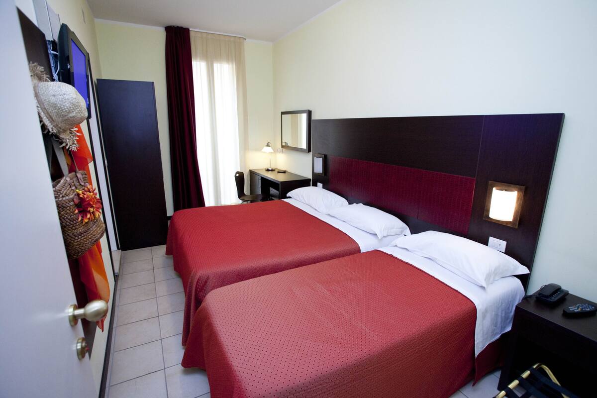 Quarto de hotel com duas camas, uma escrivaninha com luminária, um espelho e um telefone.