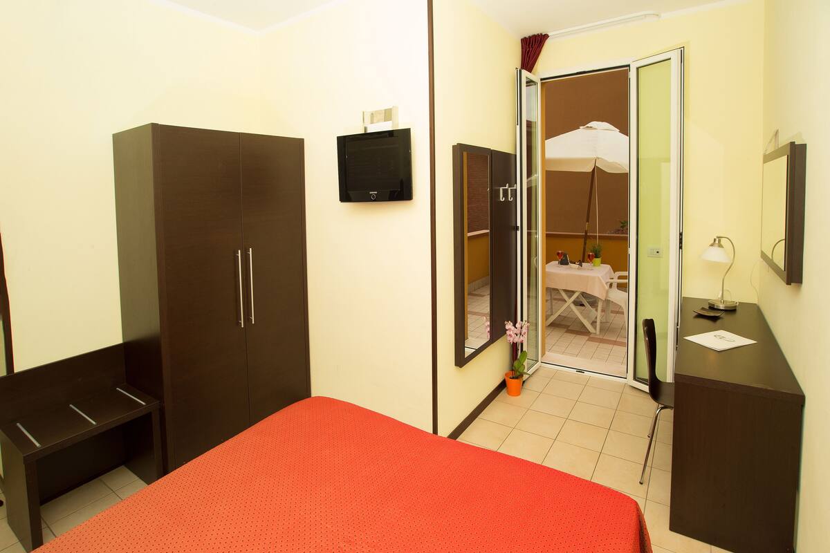 Quarto com cama, guarda-roupa, escrivaninha e uma pequena mesa com uma cadeira.