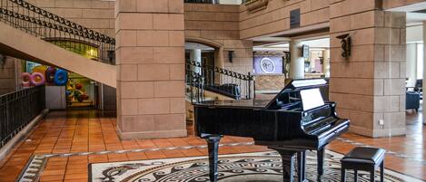 Um piano de cauda imponente num hall amplo com piso estampado, uma escadaria e uma varanda florida.