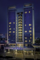 Um hotel moderno com uma entrada imponente, vários andares e janelas iluminadas.