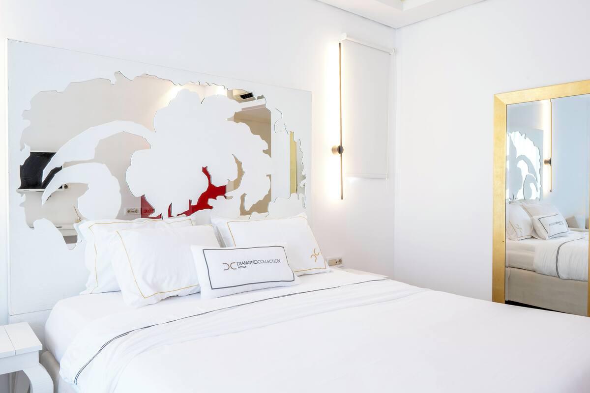Quarto de hotel moderno com uma cama grande, roupa de cama branca e uma obra de arte original na parede.