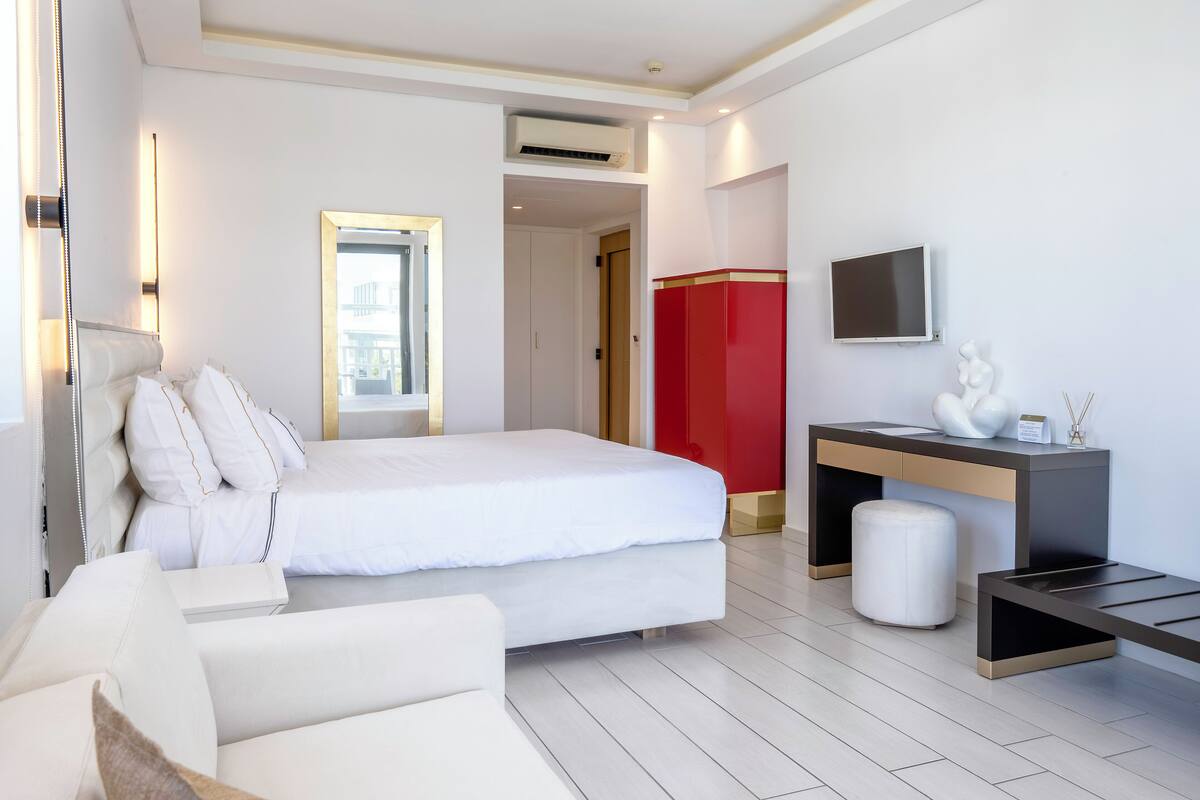 Quarto de hotel moderno com uma cama grande, uma escrivaninha, uma televisão e um guarda-roupa vermelho.