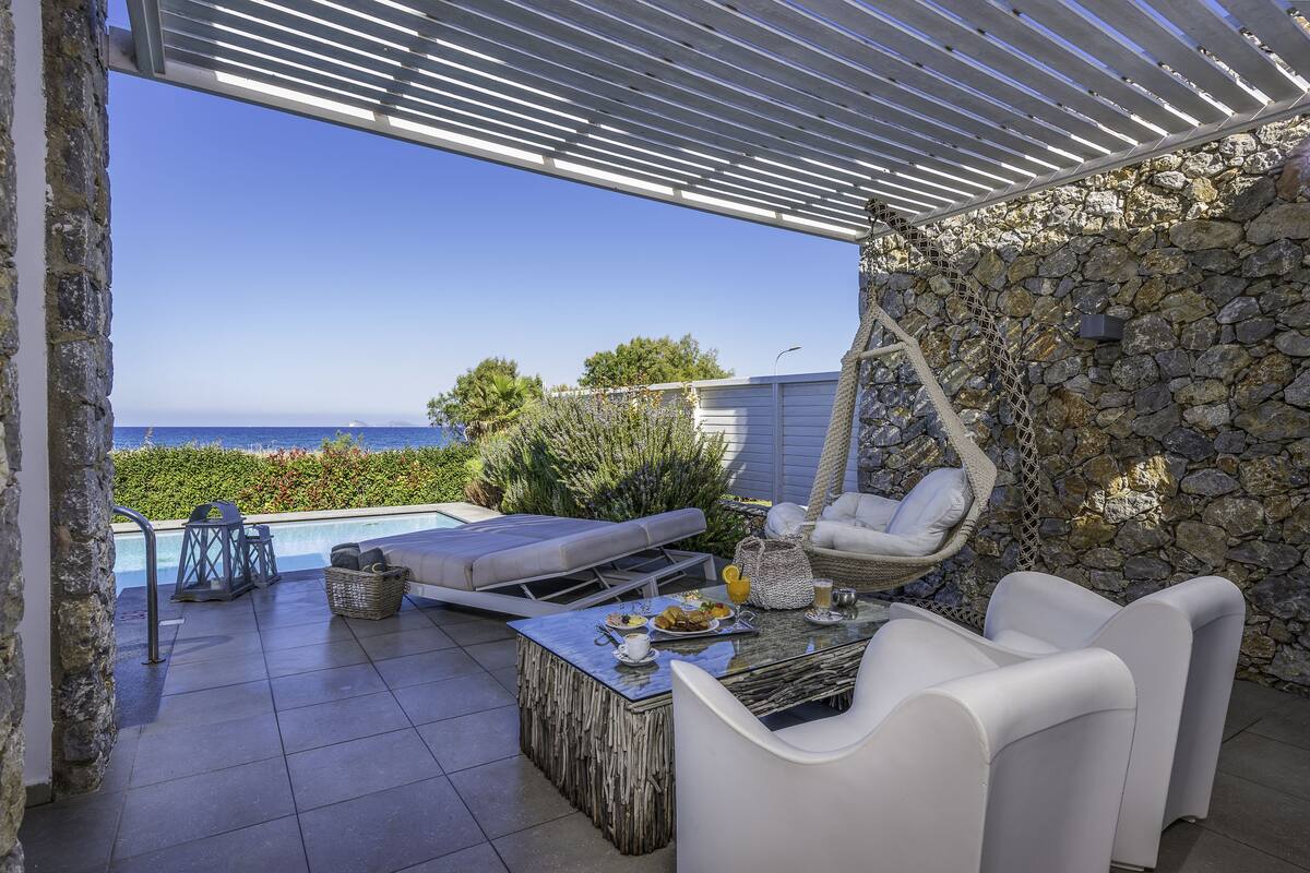 Um pátio com muro de pedra, uma cadeira suspensa, uma mesa com comida e uma piscina.