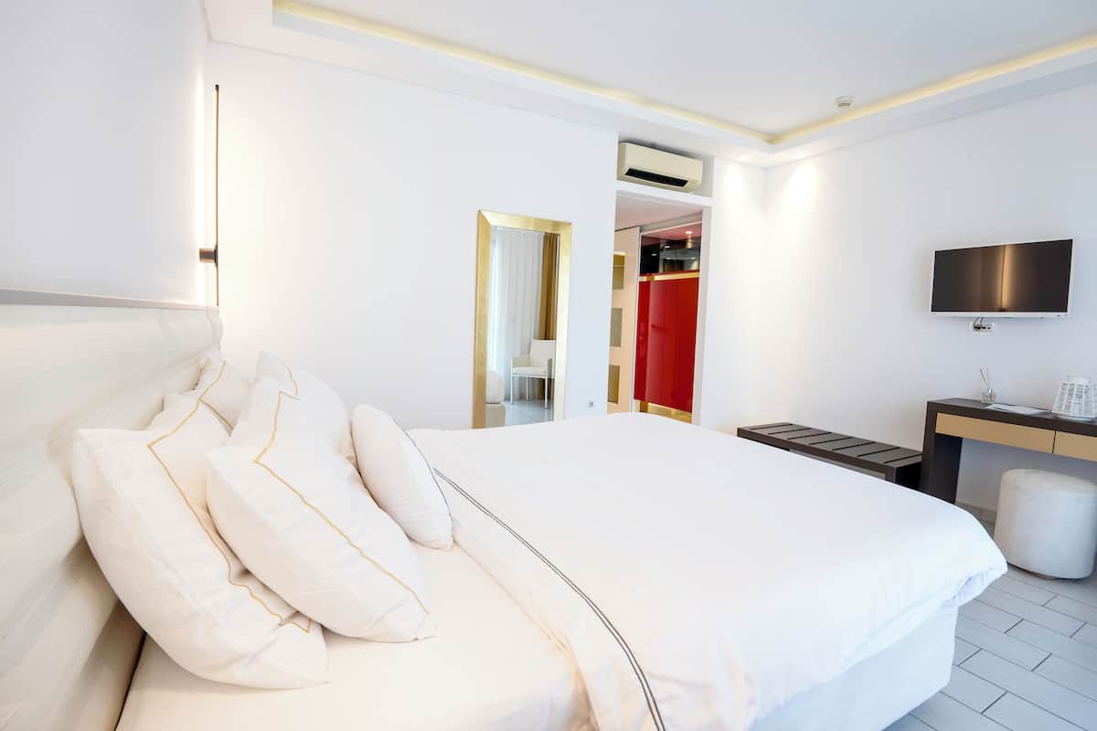 Quarto de hotel moderno com uma cama grande, uma escrivaninha, uma televisão e um aparelho de ar condicionado.