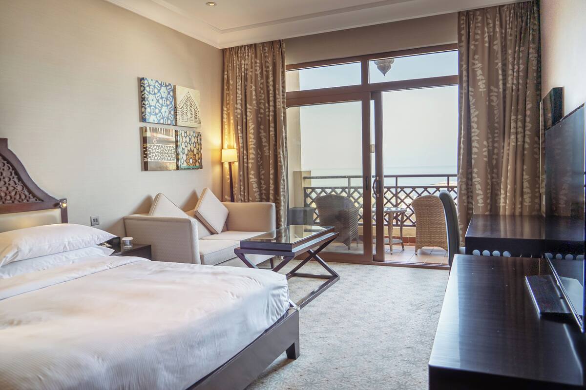 Quarto de hotel com cama, sofá, escrivaninha e varanda com vista.