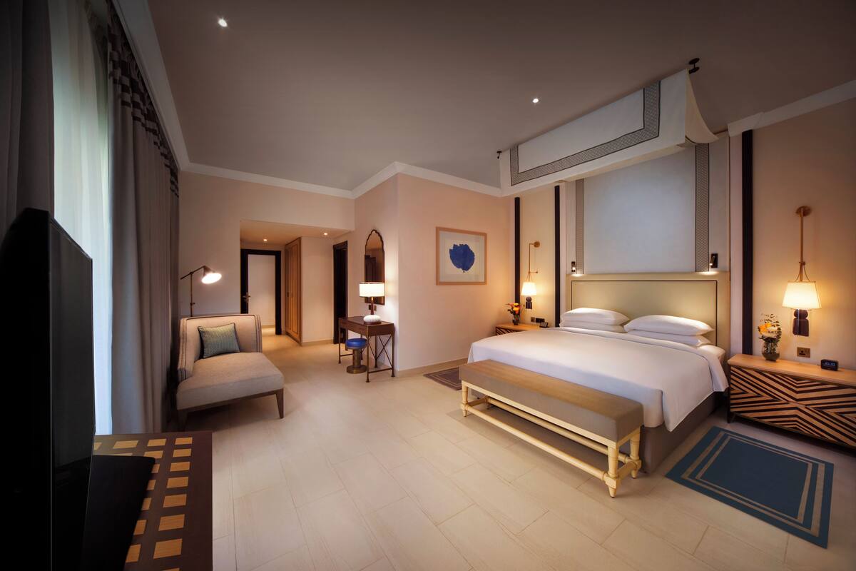 Quarto de hotel com uma cama grande, uma escrivaninha, uma cadeira e uma mesinha.