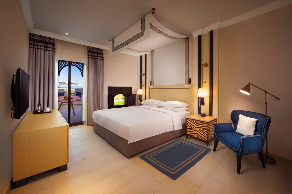 Quarto de hotel com uma cama grande, uma mesa, uma cadeira, uma televisão e vista para o exterior.