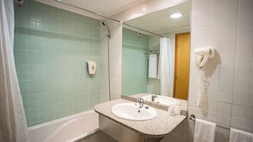 Uma casa de banho com banheira, pia, espelho e secador de cabelo fixado na parede.