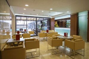 Uma área de estar moderna em ambiente interno, com mesas e cadeiras, um bar com balcão e vista para uma piscina externa.