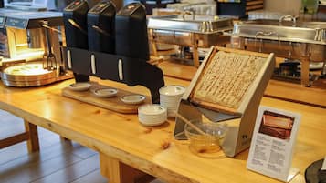 Disposição de buffet com diversas estações de comida, incluindo uma chapa, um aplicador de mel e um letreiro com os itens do cardápio.
