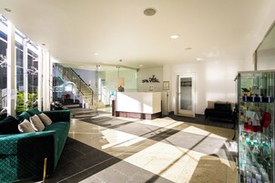 Um hall de hotel com uma mesa de recepção, uma escada e um sofá verde.
