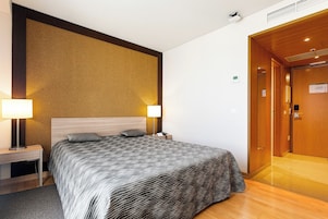 Quarto de hotel com cama, luminárias de cabeceira, mesa de cabeceira, porta de madeira e parede com textura.