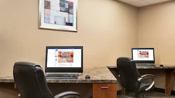 Duas mesas de escritório com computadores, cadeiras e um quadro na parede.