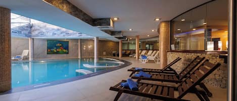Piscina interna com espreguiçadeiras e um mural na parede.