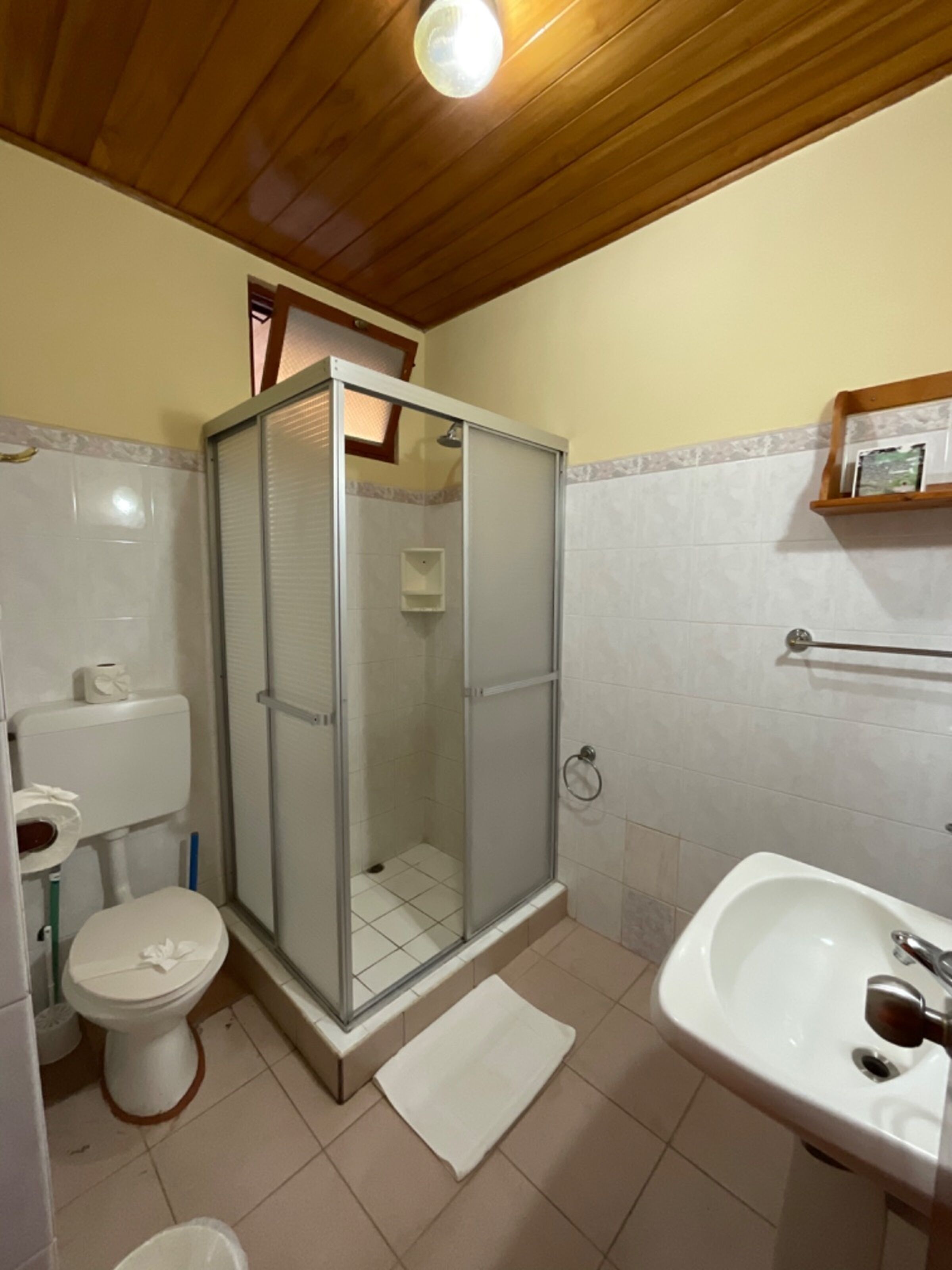 Casa de banho com cabine de duche, sanita, lavatório e toalha no chão.