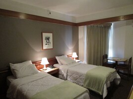 Quarto de hotel com duas camas, uma escrivaninha e uma cadeira.