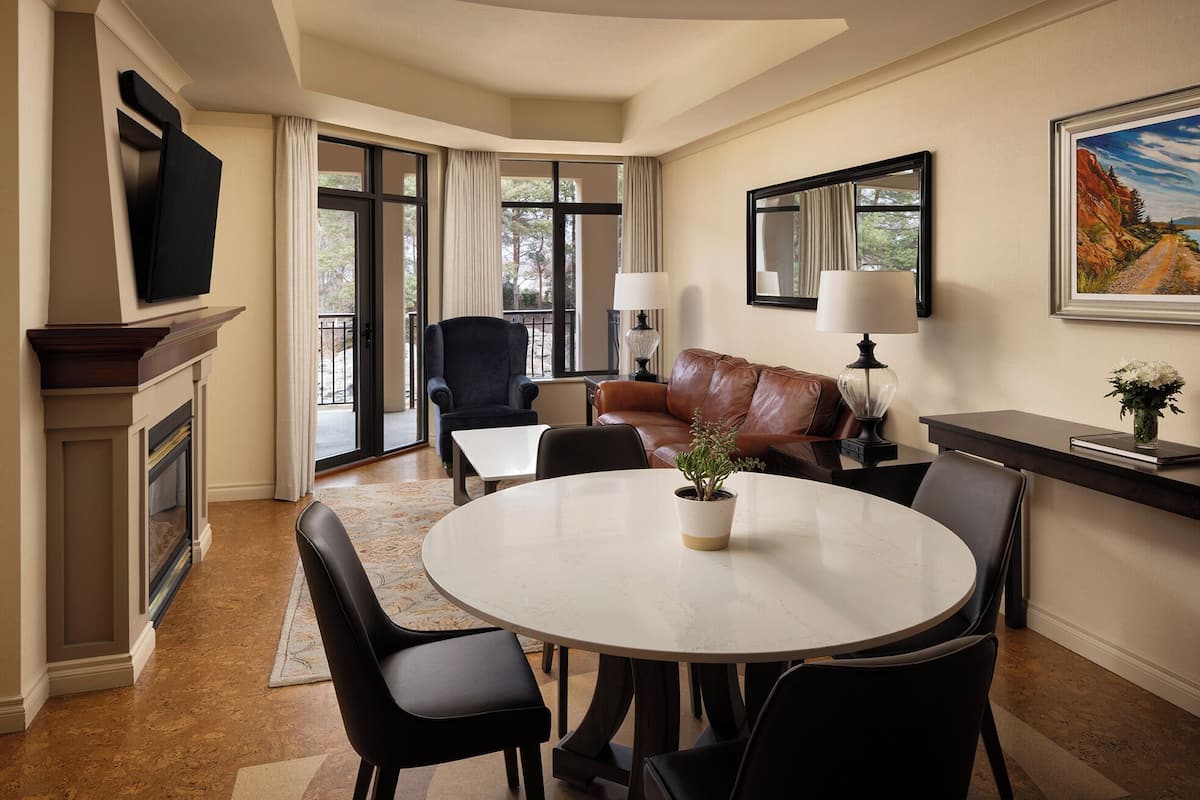 Quarto de hotel com uma mesa de jantar redonda, um sofá de couro marrom, uma televisão de tela plana fixada na parede e um quadro sobre o sofá.