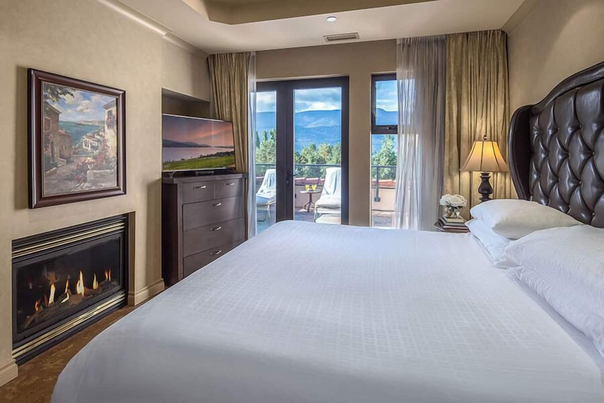 Quarto de hotel com cama grande, lareira, televisão e varanda com vista panorâmica.