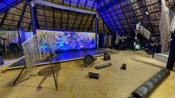 Um interior com palco, cadeira suspensa e diversos objetos no chão.