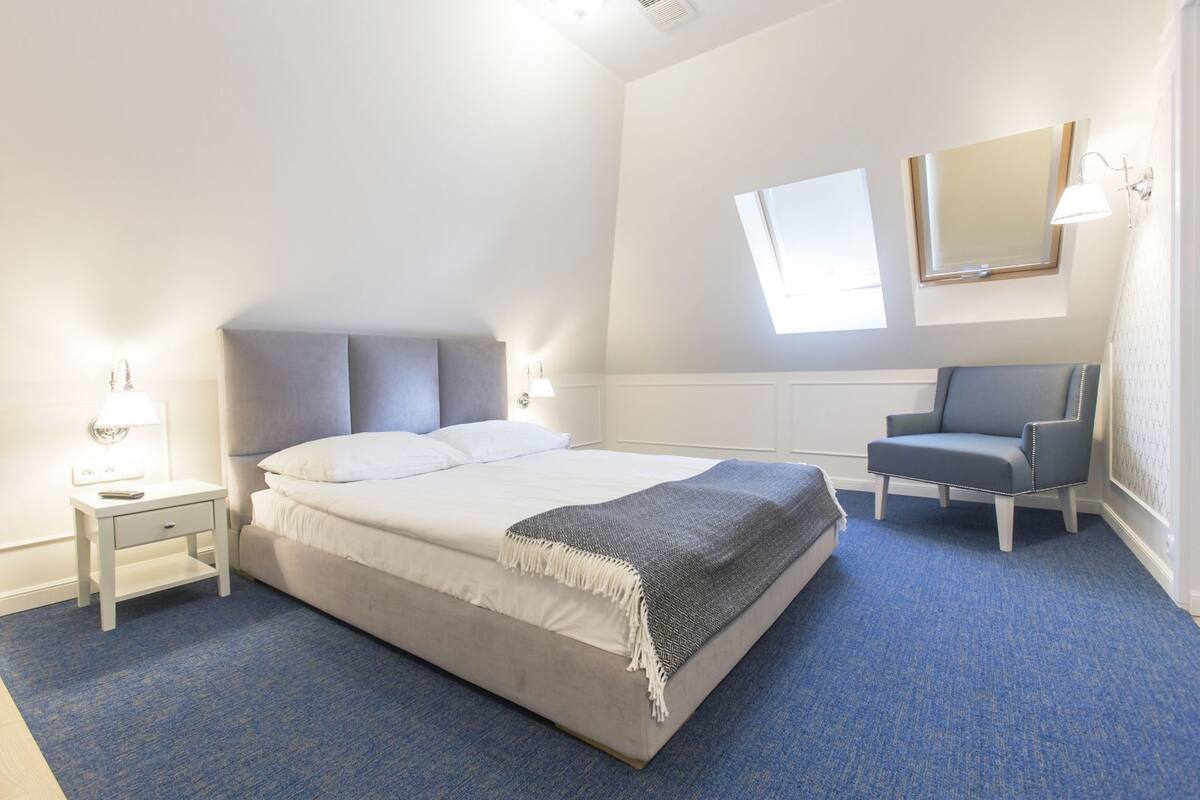 Quarto com cama, mesa de cabeceira, luminária, cadeira e janela.