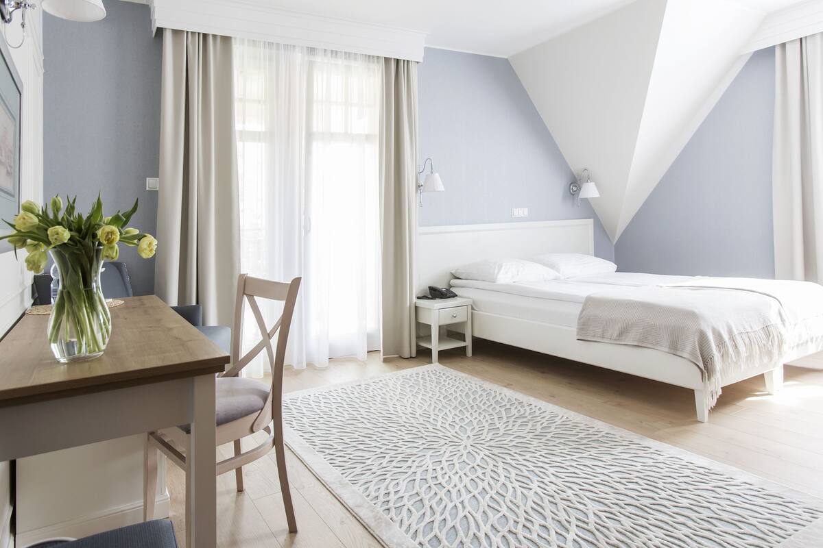 Quarto com cama, mesa de cabeceira, abajur e tapete decorativo.