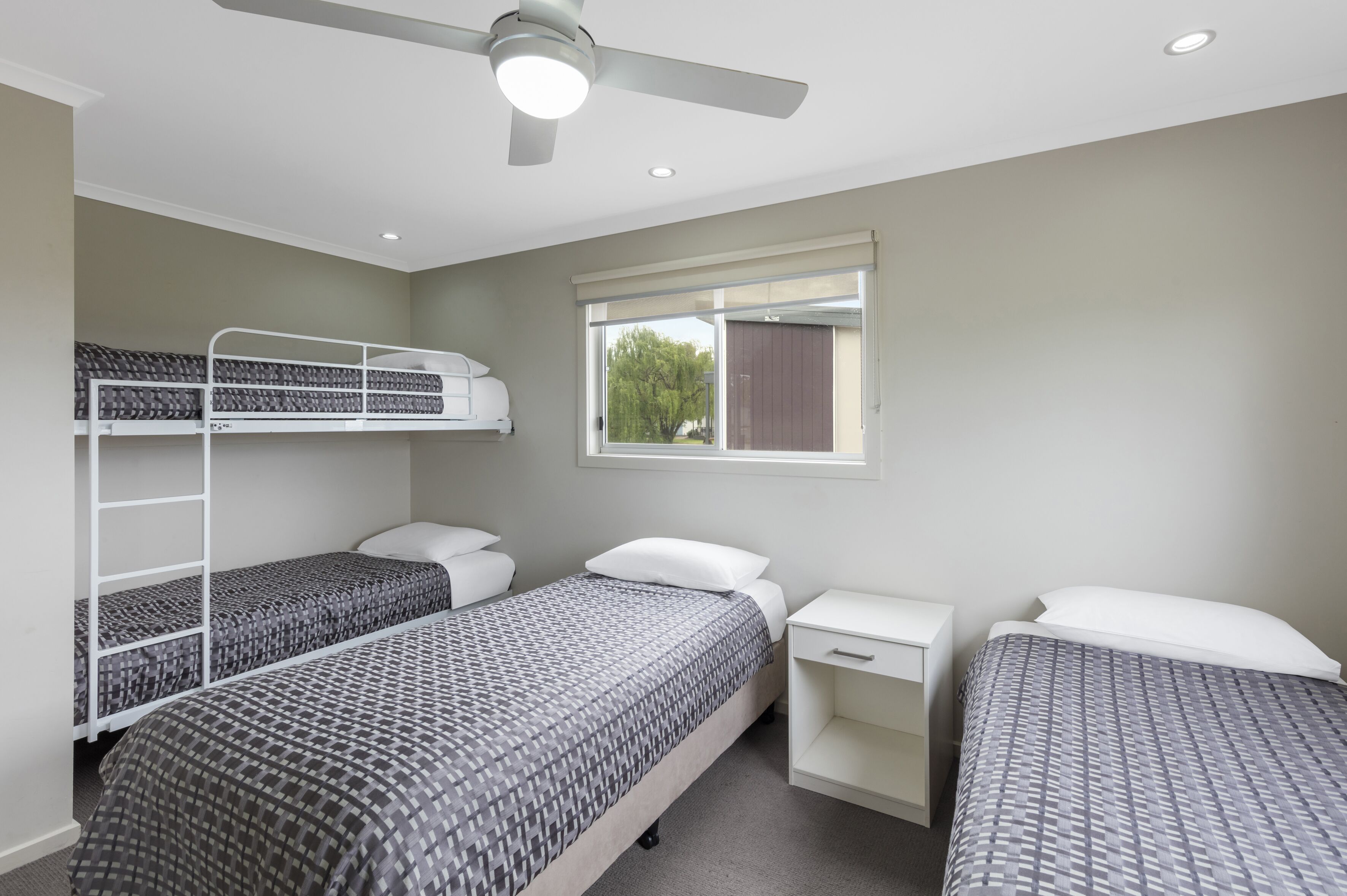 Quarto com beliches, ventoinha no teto, janela com vista e mesa de cabeceira.