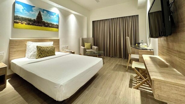 Quarto de hotel moderno com uma cama grande, uma escrivaninha, uma cadeira, uma televisão e um quadro de um templo.