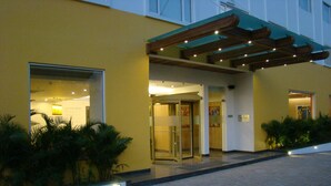 Entrada de hotel com porta de vidro, galeria coberta e calçada de azulejos.