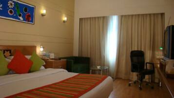 Quarto de hotel com cama, escrivaninha, cadeira, televisão e janela com cortinas.