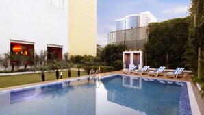 Uma piscina com espreguiçadeiras, um edifício de design moderno e um jardim bem cuidado.