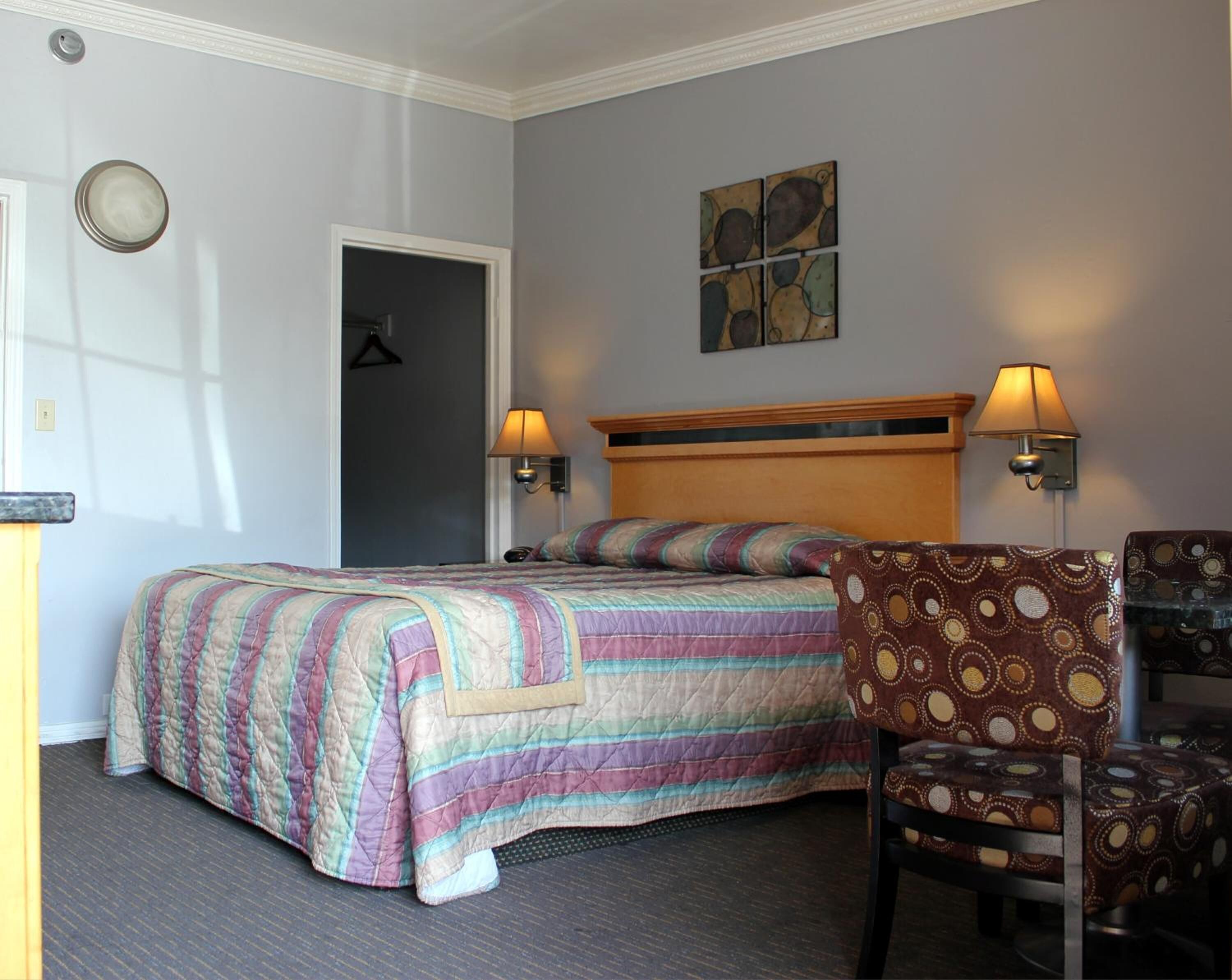 Quarto de hotel com cama, duas luminárias de parede, uma cadeira e um quadro na parede.