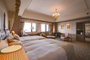 Quarto de hotel com duas camas grandes, um candelabro, uma mesa de jantar e vista para a cidade.