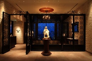 Uma área de recepção com uma estátua em pedestal, um candelabro e uma divisória iluminada em azul.