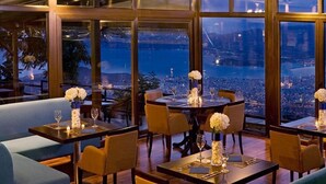 Restaurante com mesas preparadas para refeições, grandes janelas com vista para a cidade e design de interiores moderno.