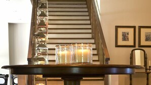 Um lustre imponente com várias velas, uma escadaria e uma mesa com velas em um ambiente iluminado.