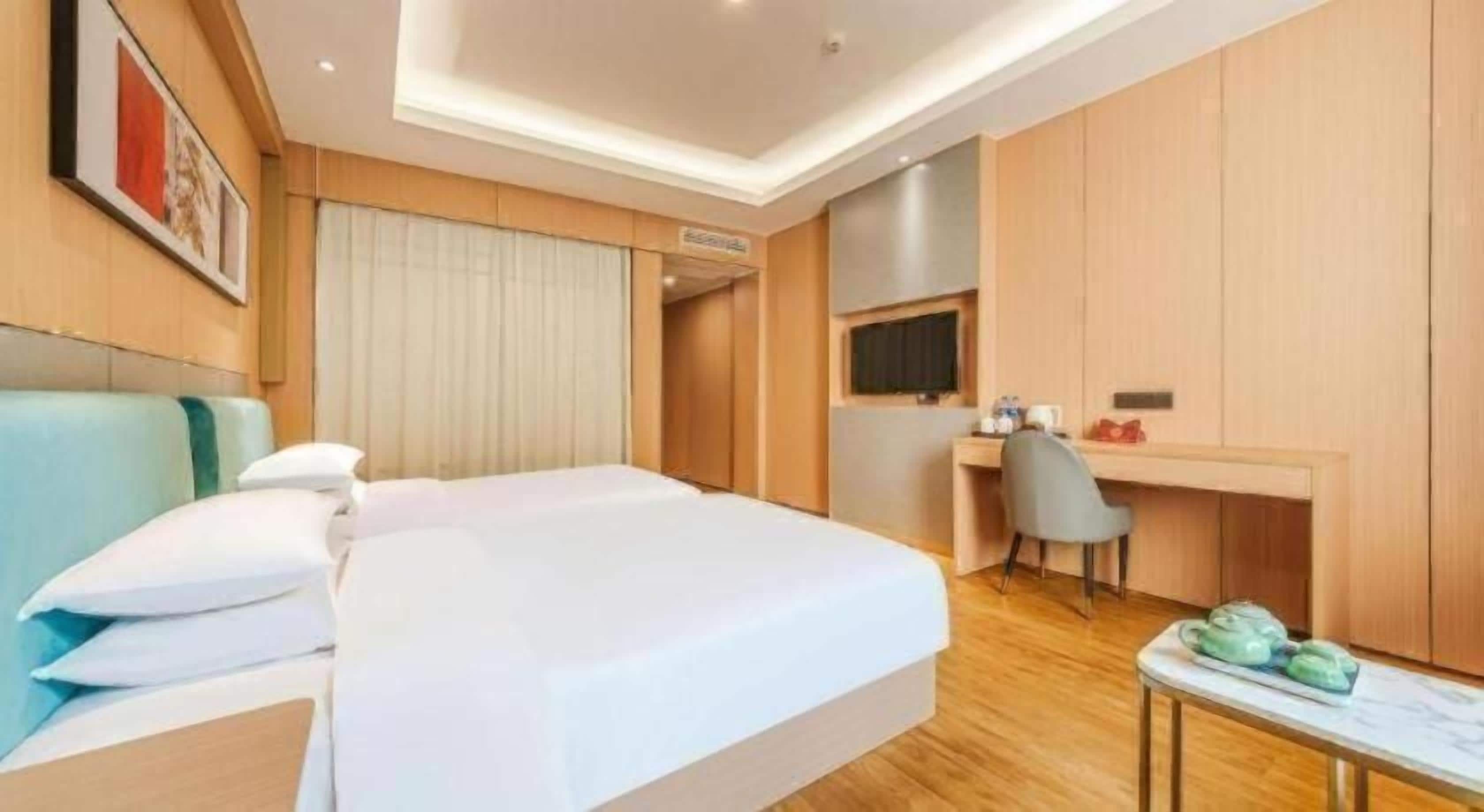 Quarto de hotel com cama, escrivaninha, cadeira e televisão.