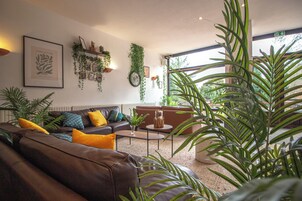 Uma sala de estar com um sofá de couro marrom, uma mesa de centro e uma janela grande com plantas.