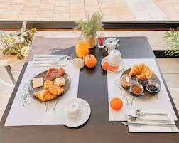 Disposição de mesa para o pequeno-almoço com croissants, queijo, fiambre e fruta, sobre um tapete de mesa.