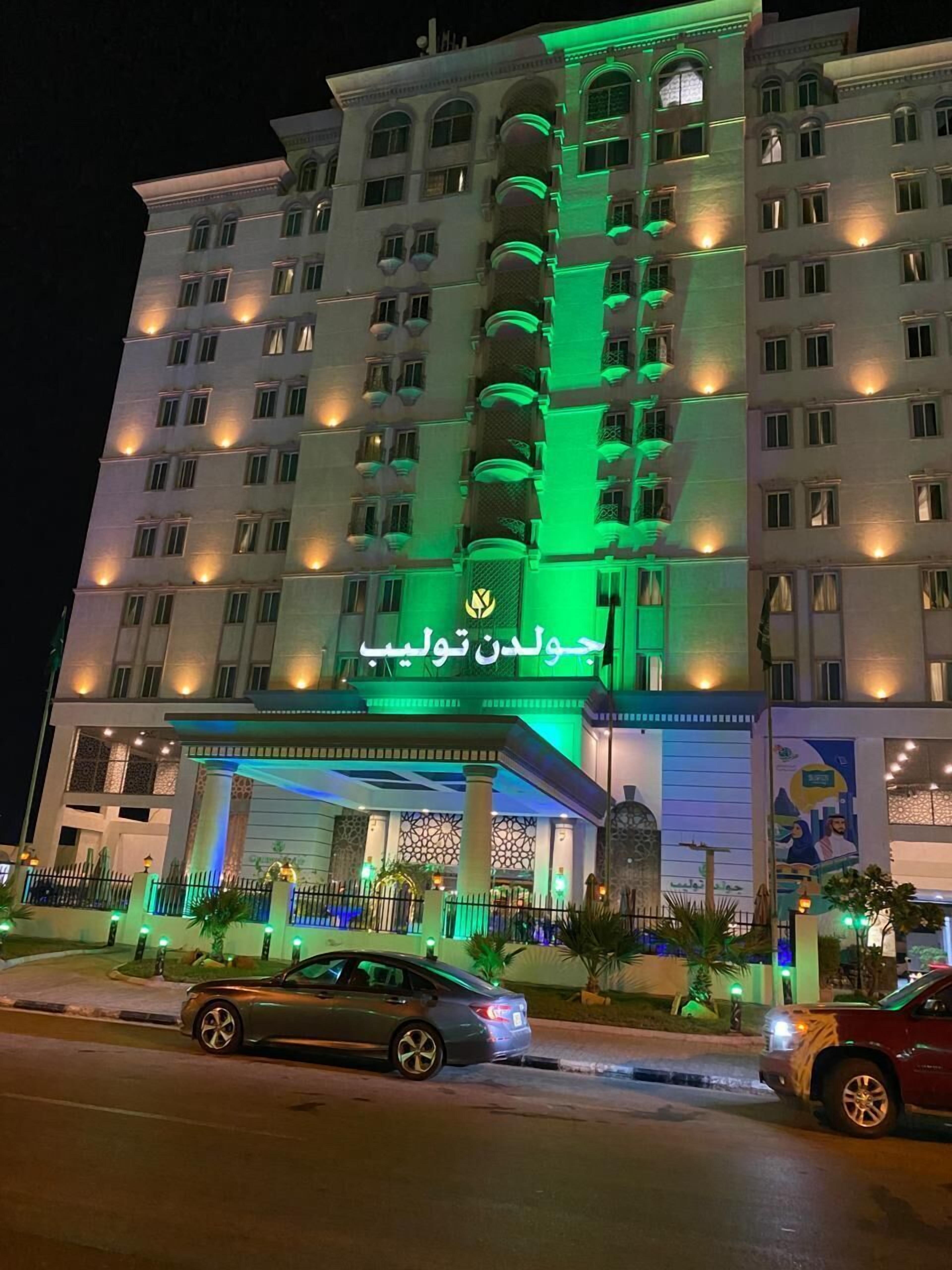 Um hotel de vários andares com uma entrada imponente e fachada iluminada em verde.